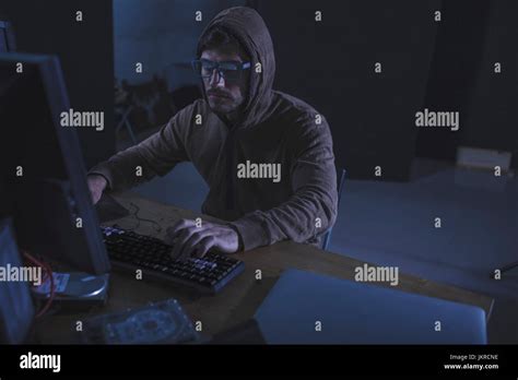 Serious Computer Hacker Wearing Hooded Shirt Using Desktop Computer At
