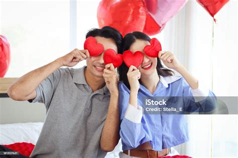 아름답게 꾸며진 침실의 흰색 침대에 앉아있는 동안 빨간 하트를 들고 눈을 가리는 행복 한 귀여운 아시아 커플 발렌타인 데이에 기념일을 축하하는 낭만적 인 연인 사랑 축하