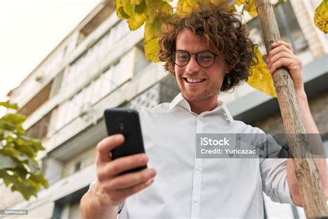 야외 서 및 스마트폰 무료 무선을 사용 하 여 실업의 하단 보기 라운드 안경 그의 휴대 전화 메시지를 읽는 보고 흰색 셔츠를