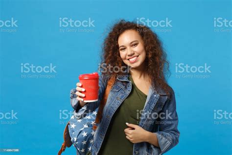 데님 옷에 젊은 아프리카계 미국인 소녀 십 대 학생 배낭 홀드 종이 컵 파란색 배경 스튜디오 초상화에 고립 고등학교 대학 대학 개념에서 교육 복사 공간을 모의 합니다 가방에