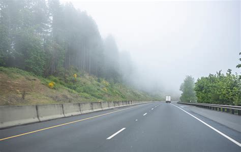 가시성이 좋지 않는 짙은 안개 날씨에 언덕에 숲이 있는 선회 하는 길 고속도로 도로에서 달리는 세미 트레일러에서 화물을 운반하는