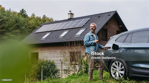 전기 자동차를 충전하는 남자 충전기를 충전 포트에 꽂습니다 그 뒤에 지붕에 태양 전지판 시스템이 있는 집 녹색 기술에 대한 스톡 사진 및 기타 이미지 Istock