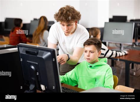 Teenager Helps Friend Solve Problem On Computer In School Class Stock