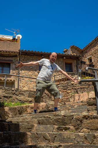 반쯤 턱수염을 기른 대머리 남자가 입을 벌리고 웃고 있고 표현력이 풍부한 눈과 팔을 뻗어 화창한 날 시골 마을의 돌계단에 서서 밝고 재미있는 놀라움을 선사한다 40 44세에