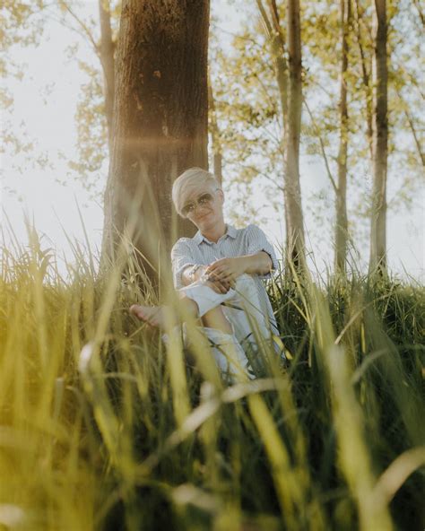 무료 사진 캐주얼 셔츠와 흰 바지를 입은 예쁜 여자가 나무 아래에 앉아 있습니다