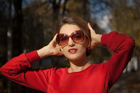 화창한 날씨에 선글라스와 빨간 스웨터를 입고 가을 공원에서 포즈를 취하고 있는 아름다운 미소 짓는 여성 가을에 대한 스톡 사진