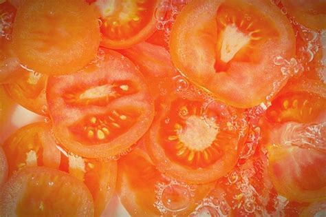 물 배경에 빨간 토마토 조각의 클로즈업 보기 유리 벽에 매크로 거품이 있는 냉각 식물성 음료의 질감 평면 디자인 0명에 대한