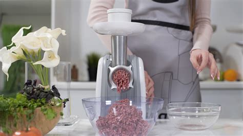 여자는 전기 고기 분쇄기에 생고기 조각을 넣습니다 다진 고기 더미 신선한 다진 고기와 전기 광부 기계 전기 고기 분쇄기로 다진 쇠고기의 준비 고기에 대한 스톡 사진 및 기타