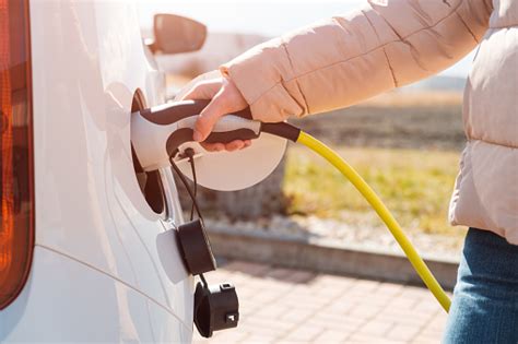 햇빛에 거리의 충전소에서 전기 자동차에 전원 공급 장치를 연결하는 여자를 닫습니다 전기 자동차 대체 연료 자동차에 대한 스톡 사진 및 기타 이미지 전기 자동차 대체 연료