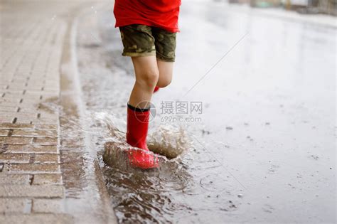 穿着红色雨靴的孩子跳进水坑特写孩子玩得开心泼水温暖的夏雨高清图片下载 正版图片505352582 摄图网