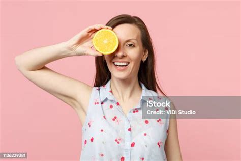 분홍색 파스텔 배경에 고립 된 신선한 잘 익은 오렌지 과일의 Halfs와 눈을 덮고 있는 여름 옷을 들고 있는 젊은 여자를 웃는 사람들은 생생한 라이프 스타일 휴식 휴가