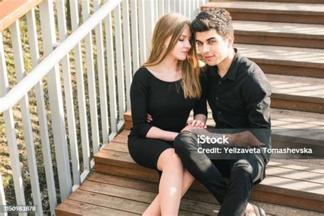 아름 다운 젊은 여러 인종 커플 사랑에 학생 부부는 도시에서 나무 계단을 앉아 있다 아름 다운 터키어 갈색 머리 남자가 검은 옷에 백인 여자를 포옹 화창한 날씨에 젊은이