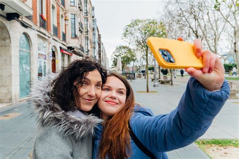 웃는 엄마와 딸이 도시의 거리를 함께 걷고 스마트폰 셀카로 행복한 순간을 포착하고 화창한 날 나들이에서 진정한 연결과 기쁨을 나눕니다 16 17 살에 대한 스톡 사진 및
