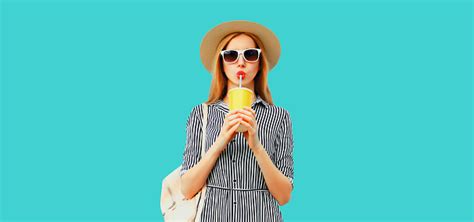 여름 밀짚 둥근 모자를 쓰고 과일 주스를 마시는 아름다운 젊은 여성의 초상화 파란색 배경에 고립된 줄무늬 드레스 20 29세에 대한 스톡 사진 및 기타 이미지 Istock