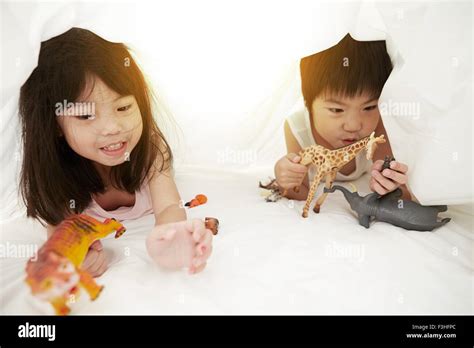 Young Chinese Boy And Girl In Bed Playing With Their Toys Under The