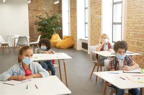 실내에서 얼굴 덮개를 착용하십시오 초등학교에서 공부하는 코로나바이러스 발병 시 보호면 마스크를 쓰고 교실 책상에 앉아 있는 학교 아이들 4 5세에 대한 스톡 사진 및 기타