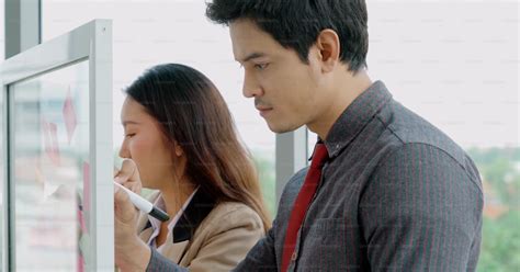 비즈니스 사람들은 사무실의 프로젝트 계획 보드에서 일하고 동료 친구와 대화하여 프로젝트 개발을 분석합니다 그들은 유리 벽에 게시 된 스티커 메모를 사용하여 정리합니다