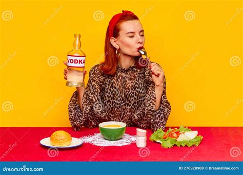 Stylish Redhead Woman Sitting At Table Against Yellow Background And