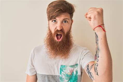 고립 된 흰색 배경 위에 서있는 티셔츠를 입은 젊은 빨간 머리 아일랜드 남자는 화가 나고 화가 나서 분노로 외치고 미친 듯이 고함치고 분노 개념으로 T 셔츠에 대한 스톡