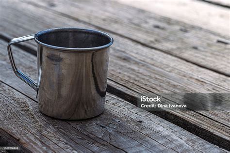 소박한 나무 테이블에 있는 스테인레스 스틸 머그잔은 야외에서 햇빛을 반사합니다 금속 커피 컵 미니멀리즘 여행 필수품 캠핑 하이킹 자연 속에서의 지속 가능한 생활 선택적 초점