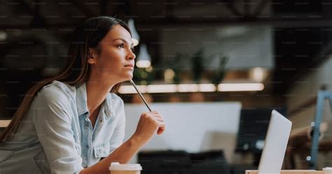 흰색 노트북으로 사무실 책상에 기대어 있는 사려 깊은 소녀의 측면 모습 초상화 그녀는 커피 한 잔을 들고 연필로 턱을 만지고