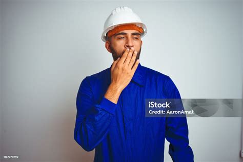 잘 생긴 인도 노동자 남자 유니폼과 헬멧 위에 고립 된 흰색 배경 지루 하품 피곤 한 손으로 입을 덮고 불안과 졸음 가리기에