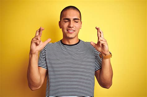 노란색 고립 된 배경 제스처 손가락 위에 줄무늬 티셔츠를 입고 젊은 잘 생긴 남자는 희망과 눈을 감고 미소 교차 행운과 미신 개념 T 셔츠에 대한 스톡 사진 및 기타 이미지