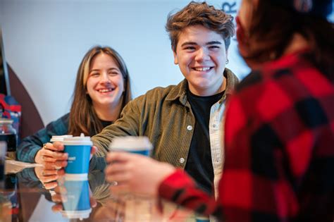 십대 소년은 카페테리아의 카운터에서 종이 컵에 커피를 마시 며 여성 친구들과 즐겁게 이야기합니다 14 15 살에 대한 스톡 사진 및 기타 이미지 Istock