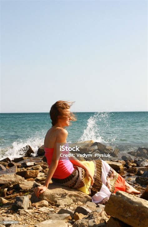 화려한 긴 치마를 입은 소녀가 바닷가의 바위 위에 앉아 있다 넓은 모래 해변에서 아름다운 화창한 날 화려한 여자 실루엣 바다 해변 휴일 휴식 사진입니다 파도가 거품을