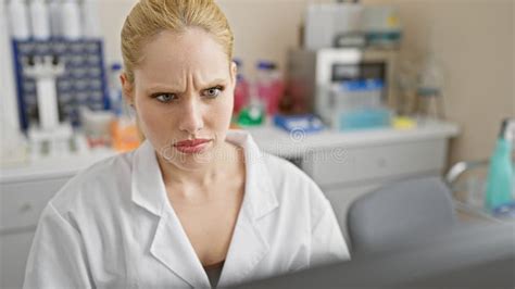 Focused Blonde Woman In A Laboratory Setting Scrutinizing A Computer