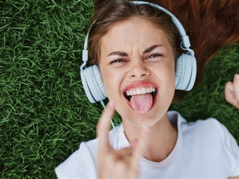 девочка подросток слушающая музыку в наушниках лежащую на зелёной траве в парке улыбаясь и