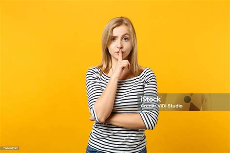 줄무늬에 예쁜 젊은 여자 말하는 자장은 입술 쉿 제스처 노란색 오렌지 벽 배경에 고립에 손가락으로 조용 합니다 사람들은 진심으로 감정 라이프 스타일 개념입니다 복사 공간을