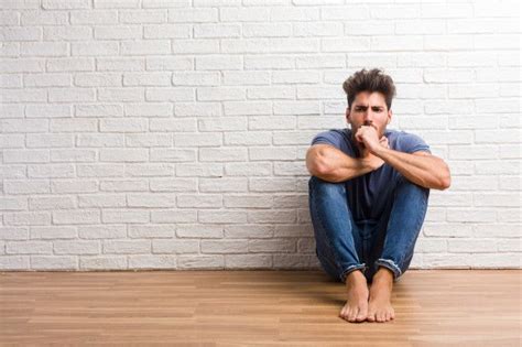 Молодой естественный человек сидит на деревянном полу с ангиной больной из за вируса Премиум