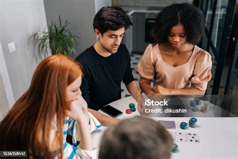 주말에 홈 파티를 하는 다민족 친구들이 거실 테이블에 앉아 포커를 하는 모습 재미를 즐기는 백인과 아프리카 사람들 놀이에 대한 스톡 사진 및 기타 이미지 Istock