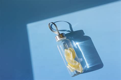 레몬 물은 병에 담긴 해독을 마시고 푸른 배경에 햇빛을 쬐며 그림자를 드리운다 건강 다이어트 건강한 식습관 탑 뷰 유리 재사용 가능한 물병 친환경 라이프 스타일 최소한의