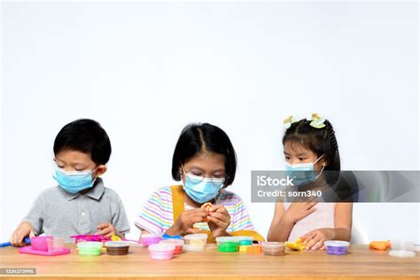 흰색 배경이있는 나무 테이블에 점토 장난감을 함께 연주하는 동안 얼굴 마스크를 착용 하는 아시아 어린이 아이들의 새로운 정상