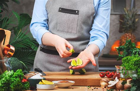 부엌에서 음식을 요리합니다 요리사는 얇게 썬 라임을 들고 있습니다 나무 테이블 주방용품 야채 허브 및 재료 건강한 비건 채식 요리법 블로깅 감귤류 과일에 대한 스톡 사진 및