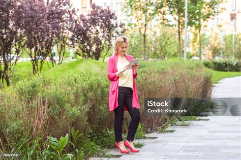 녹색 공원에 서 있는 우아한 스타일의 행복 한 아름 다운 젊은 성공적인 블로거 사업가의 전체 길이 초상화 이빨 미소와 타이핑 메시지와 태블릿을 들고 거리에 대한 스톡 사진