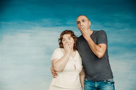 통통한 빨간 머리의 매력적인 여자와 파란색 배경에 키가 큰 대머리 남자는 감정적으로 그들이 본 것에 놀라게된다 그들은 카메라를