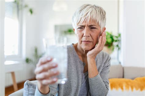민감한 치아를 가진 수석 여성과 얼음으로 차가운 물 한 잔을 들고 있는 손 헬스케어 개념 차가운 음료를 마시는 성숙한 여자 얼음 큐브의 전체 유리와 치통 통증을 느낀다