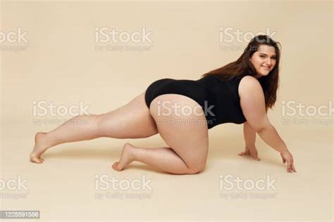 플러스 크기 모델 뚱뚱한 여자 에 검정 바디 수트 초상화입니다 베이지 색 배경에 포즈 갈색 머리를 크롤링 신체 긍정적 인 개념 기어가기에 대한 스톡 사진 및 기타 이미지