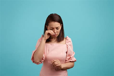 얼마나 슬픈지 어두운 머리와 분홍색 드레스에 닫힌 눈을 가진 우울한 유럽 여성은 눈물을 닦아 뺨을 만지고 얼굴 표정과 파란색 배경에 고립 된 해결할 수없는 문제를
