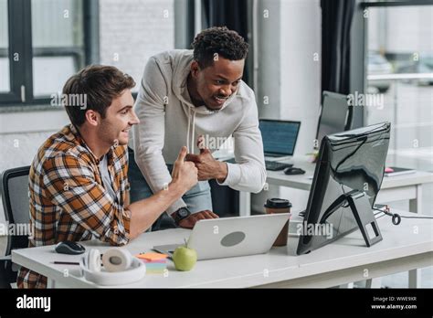 Two Cheerful Multicultural Programmers Showing Thumbs Up While Looking At Computer Monitor Stock