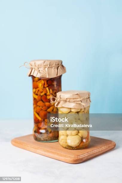 맛있는 수제 절인 꿀 버섯을 곁들인 두 개의 유리 항아리 향신료가 있는 샴페인 나무 판에 채식 발효 음식 밝은 파란색 배경 야채