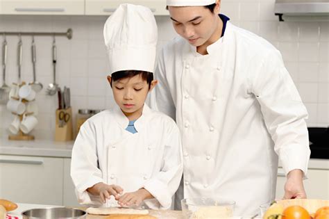 모자를 쓴 요리사 유니폼을 입은 행복한 아시아 아들과 아버지는 부엌에서 함께 식사를 요리하고 아빠 부모와 소년 아이는 빵 반죽을 준비하고 귀여운 가족은 베이커리 음식을