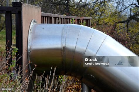 잔디 언덕과 나무 팔리세이드가있는 필드에 스테인레스 스틸 슬라이드 타탄 고무 패드에 영향을 미치는 어린이를 슬라이딩하기위한 대형 광택 튜브 튜브의 끝은 열린 쓰루입니다 0