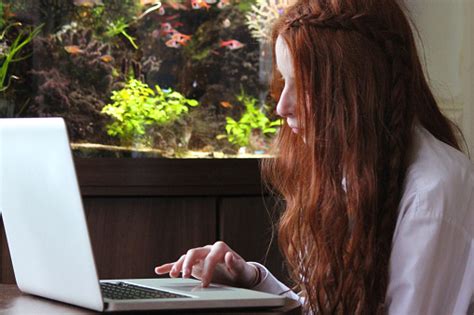 창백한 피부와 주근깨가있는 빨간 머리 십대 소녀 14 15의 이미지는 가정 사진에서 작업하는 노트북 컴퓨터에서 작업하는 가정용 방의 테이블에 앉아있었습니다 교복에 대한 스톡