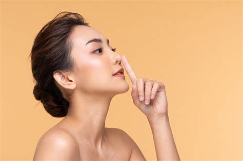 깨끗하고 신선한 피부 행복과 베이지 성형 수술 코 뷰티 화장품 및 스파 얼굴 치료 개념에 긍정적 인 감정으로 명랑코 미소를 만지는 아름다운 아시아 여성 메이크업 화장품에