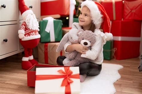 Adorable Hispanic Girl Hugging Teddy Bear Sitting On Floor By Christmas