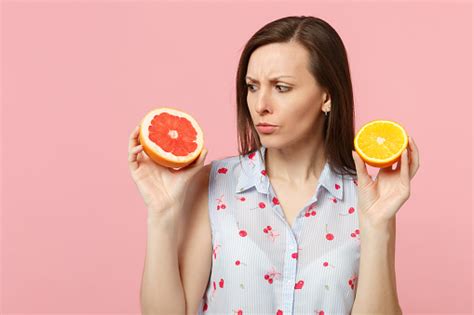 분홍색 파스텔 벽 배경에 고립 된 신선한 익은 자 몽 오렌지 과일의 Halfs를 들고 여름 옷에 관련 된 젊은 여자 사람들은 생생한 라이프 스타일 휴식 휴가 개념입니다 복사